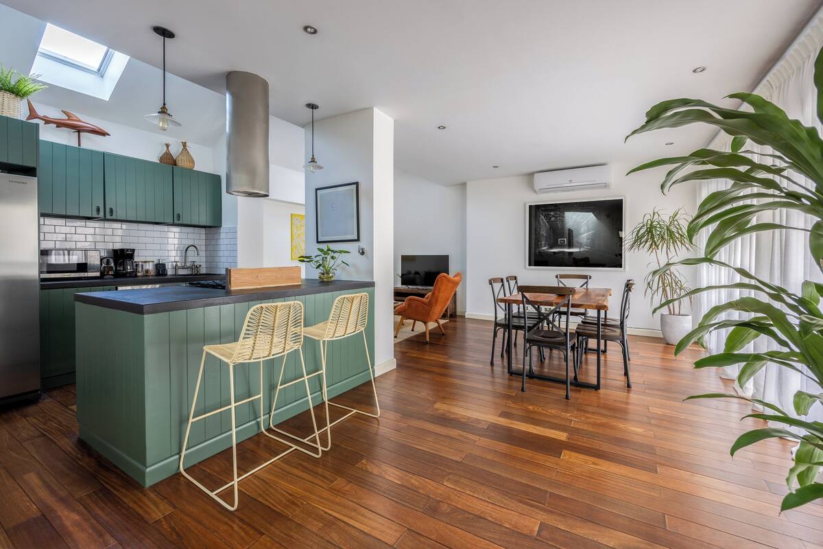 Cozinha moderna com ilha central, banquetas e área de jantar com televisão.