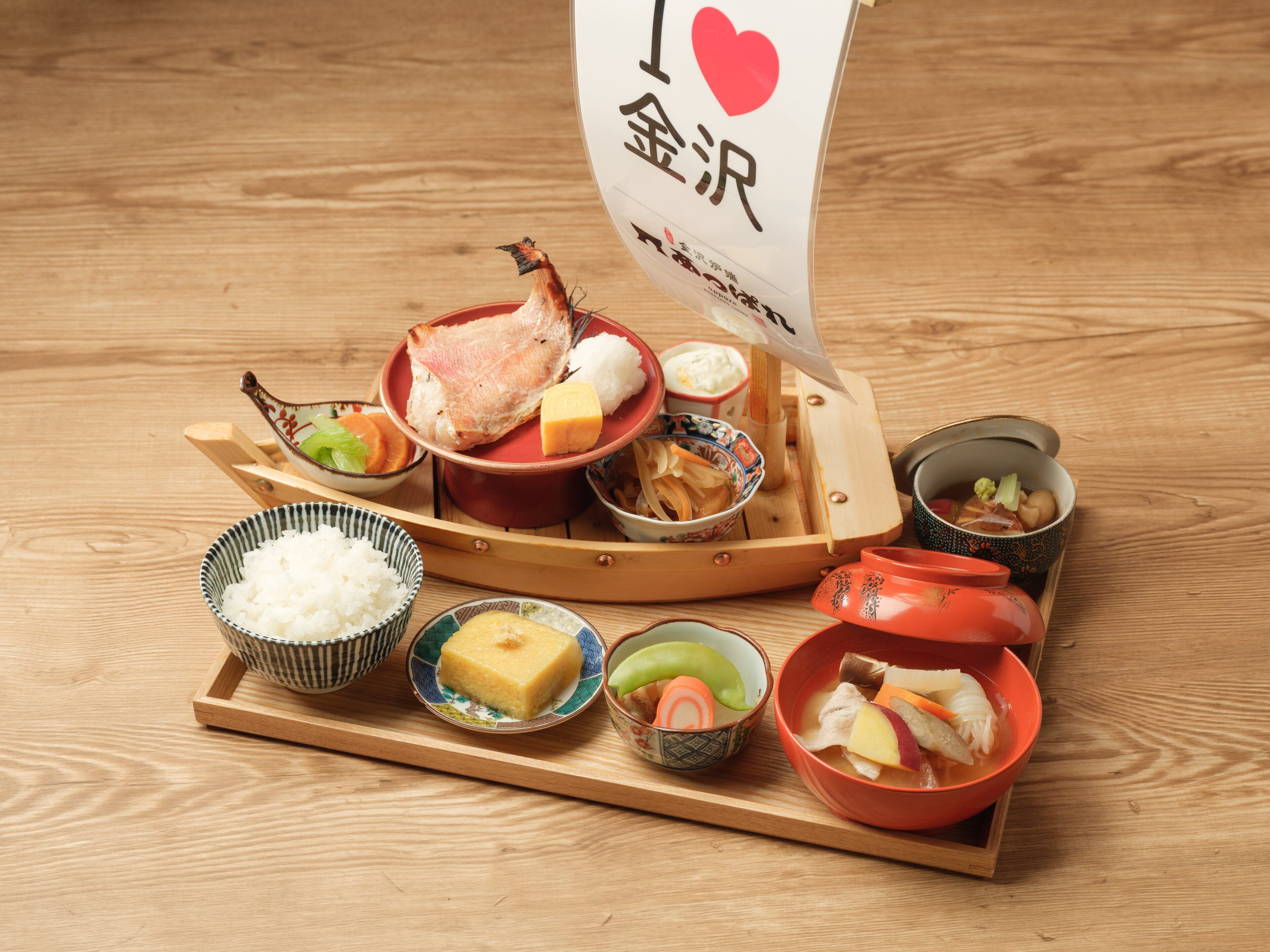 Uma refeição tradicional japonesa com diversos pratos, incluindo arroz, peixe e legumes, servida em uma bandeja de madeira.