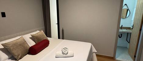 Quarto com cama, almofadas, toalha e piso de madeira.