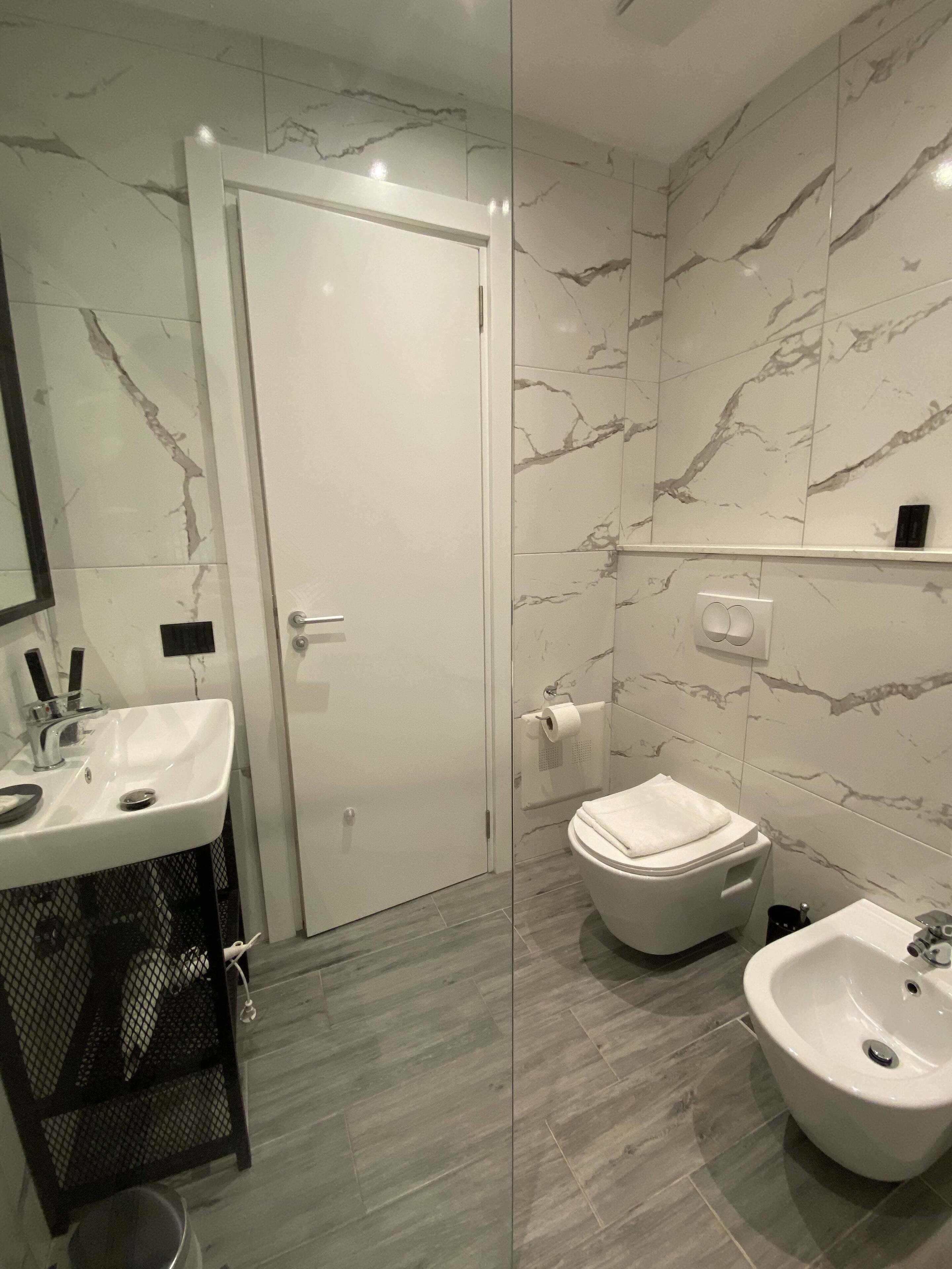 Um banheiro moderno com porta branca, pia com espelho, vaso sanitário e bidê.