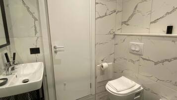 Um banheiro moderno com porta branca, pia com espelho, vaso sanitário e bidê.