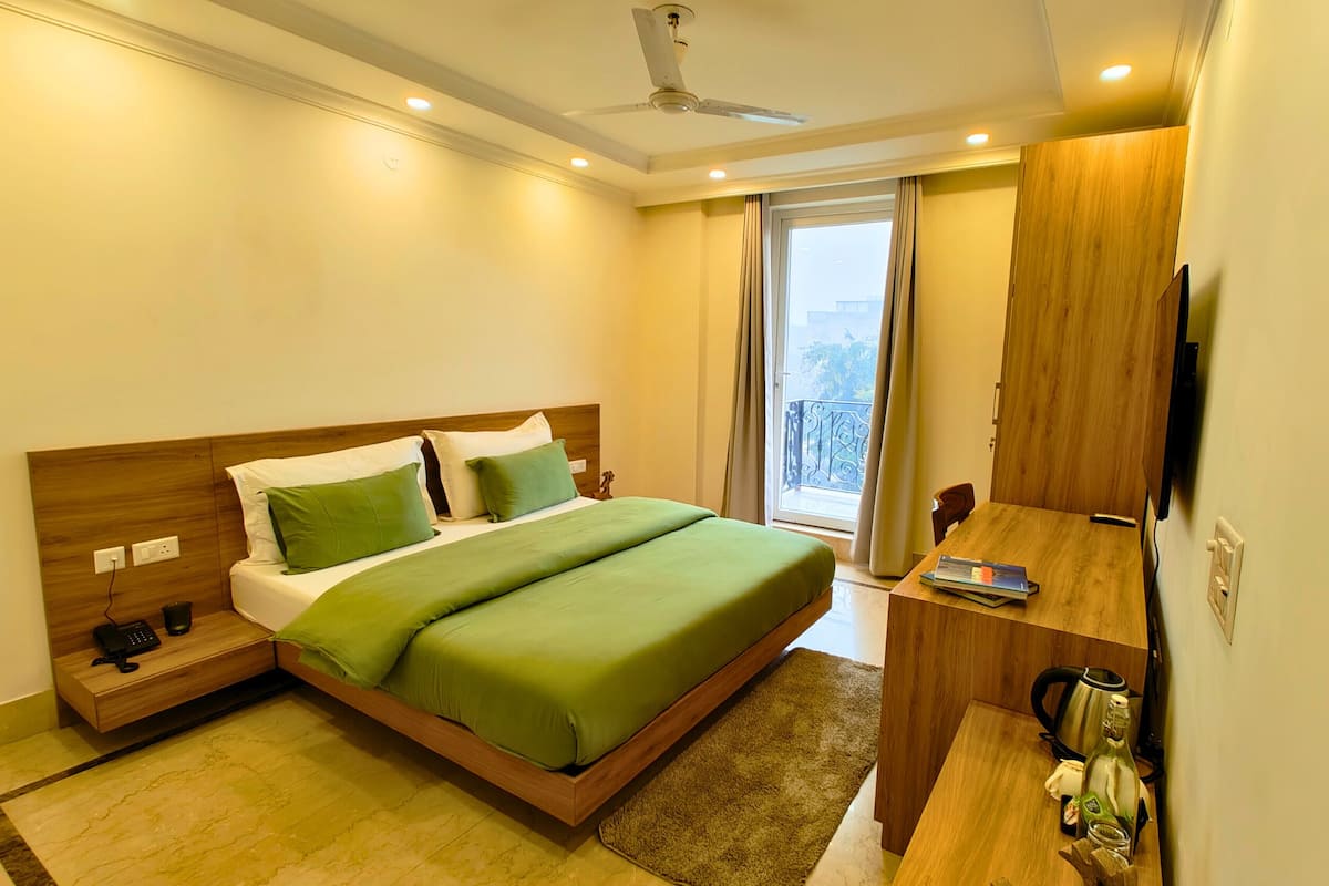 Quarto de hotel moderno com cama de madeira, roupa de cama verde, uma pequena escrivaninha com chaleira e televisão.