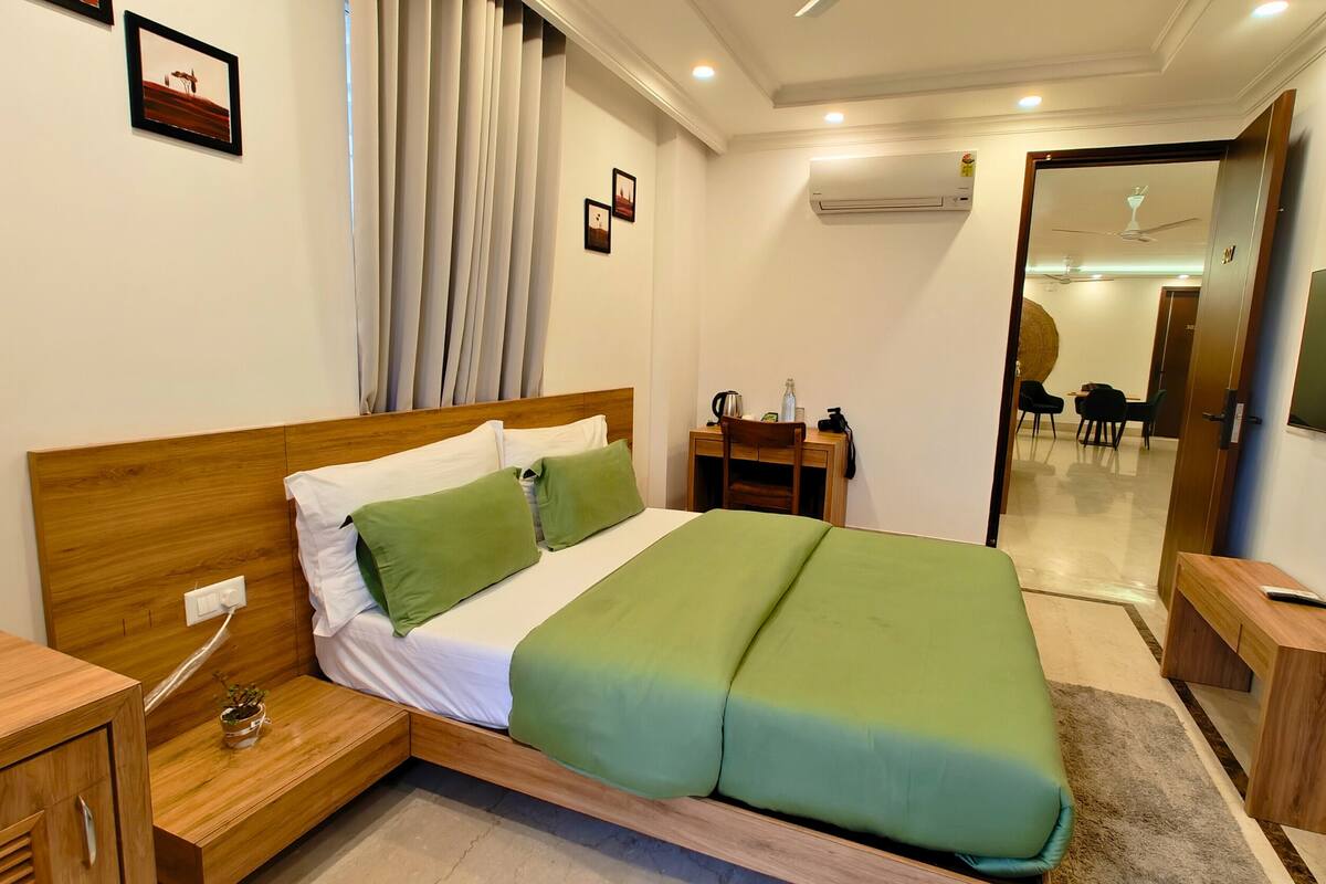 Quarto de hotel com cama de madeira, uma escrivaninha, uma cadeira, televisão e espelho.