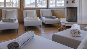 Quarto com três sofás brancos, lareira e amplas janelas com vista para a neve.