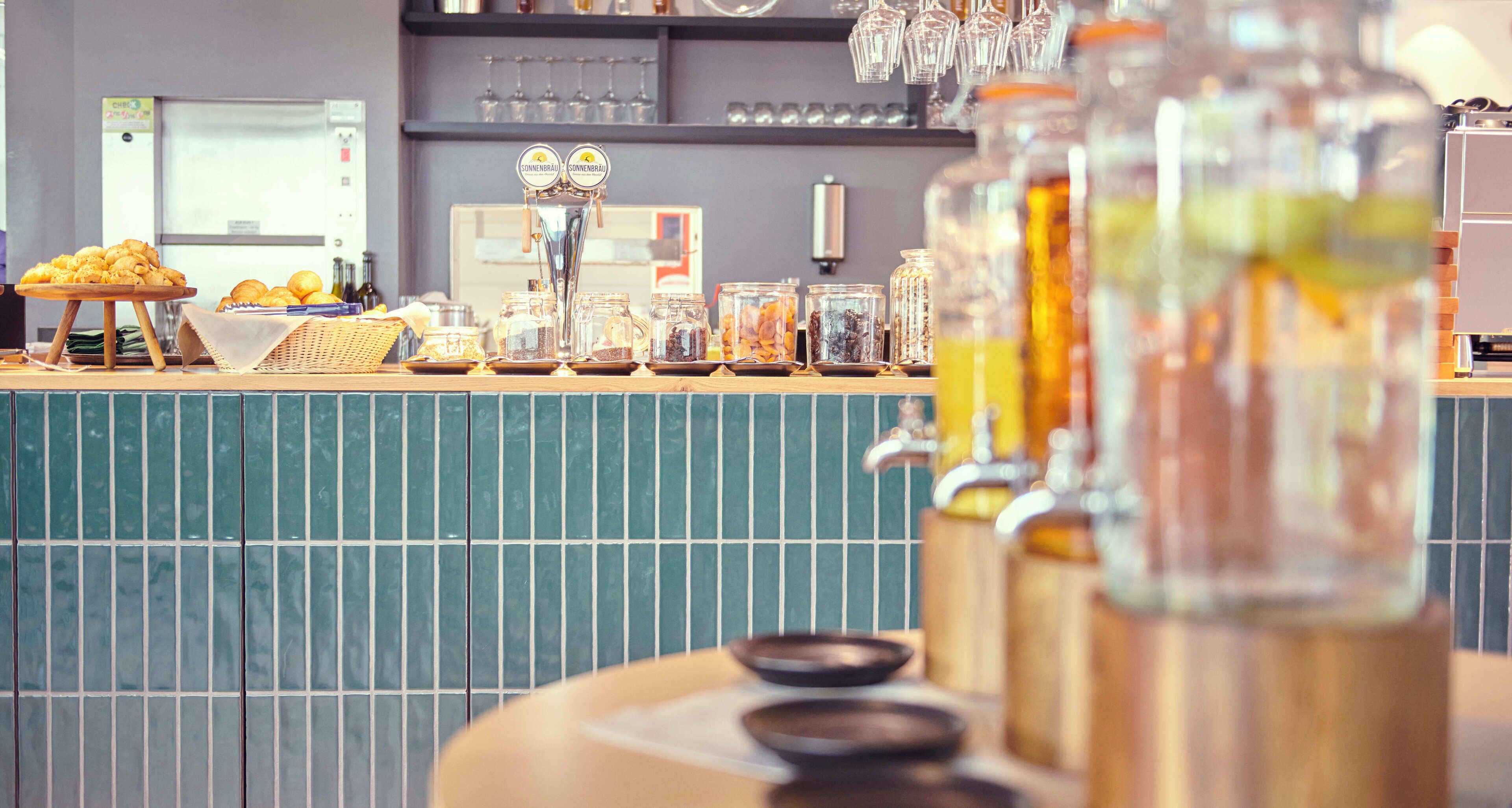 Uma área de bar com balcão exibindo alimentos, uma torneira de cerveja e diversos recipientes de vidro.