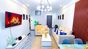 Uma sala de estar moderna com uma televisão de tela plana, um sofá, uma mesa de centro e um espaço de jantar com mesa posta para dois.