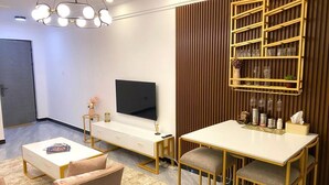 Uma sala de estar moderna com televisão, sofá, mesa de centro e um espaço de jantar com banquetas.