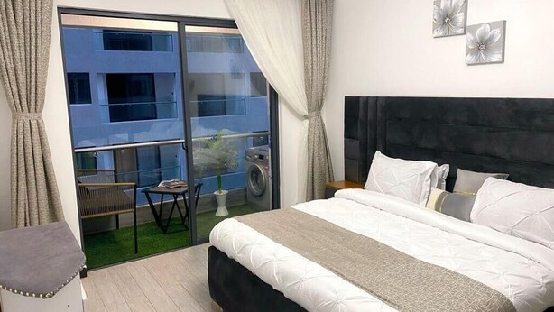 Quarto de hotel com uma cama grande, uma varanda com vista para um edifício e uma pequena mesa com uma cadeira.