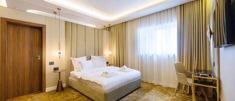 Quarto de hotel com uma cama grande, uma escrivaninha com cadeira, televisão e janela com cortinas.