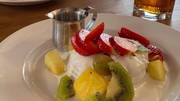 Um prato de sobremesa com frutas e um pequeno jarro de metal sobre uma mesa.