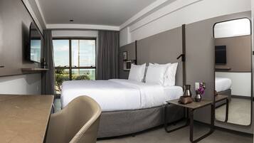 Quarto de hotel com cama grande, escrivaninha, cadeira, televisão e varanda com vista.