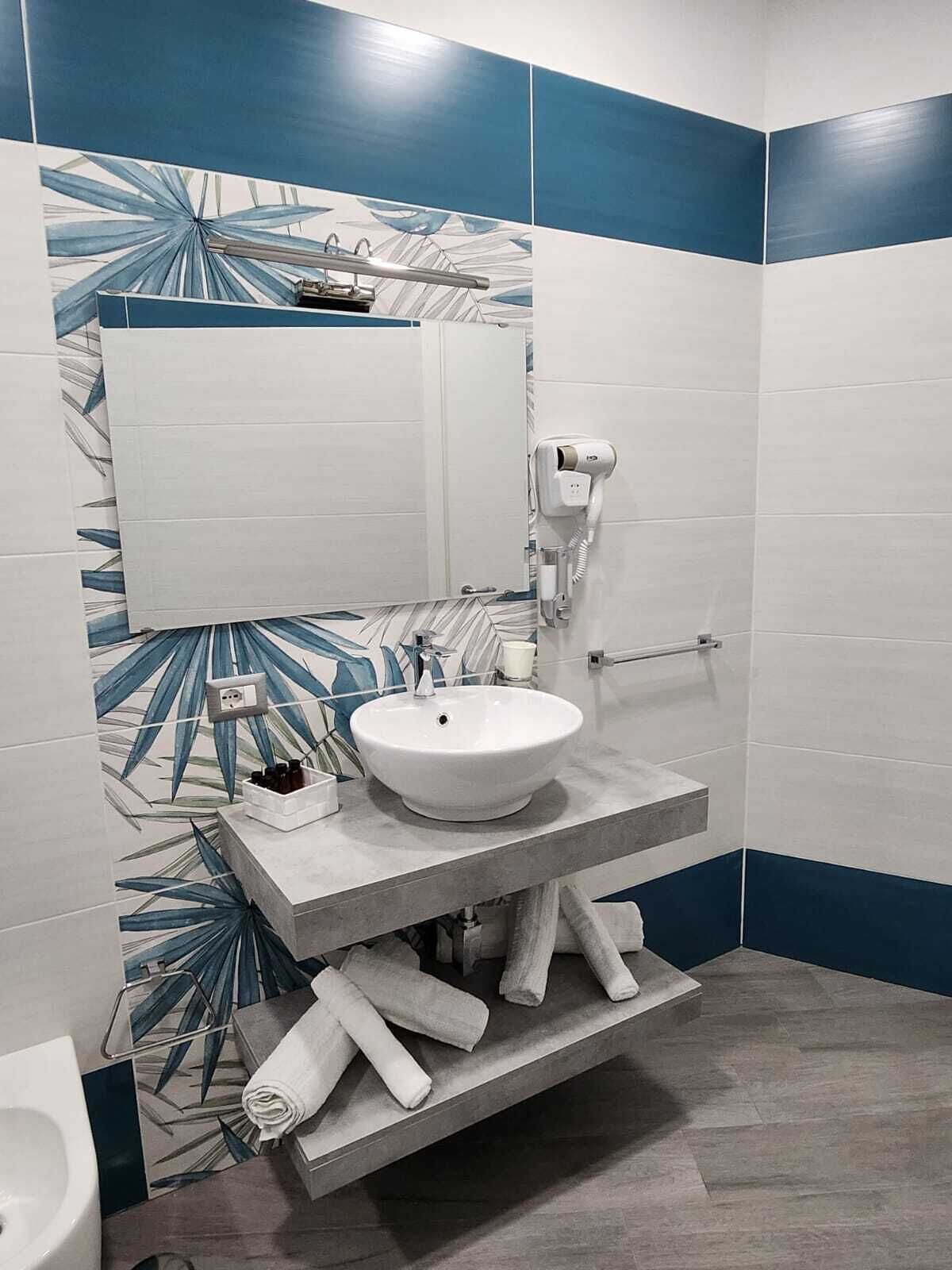 Casa de banho com uma pia branca, um espelho, um porta-toalhas e um secador de cabelo.