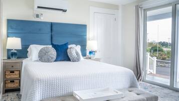 Quarto de hotel com uma cama grande, duas mesas de cabeceira com luminárias, vista para o exterior por uma janela ampla e um ar condicionado na parede.