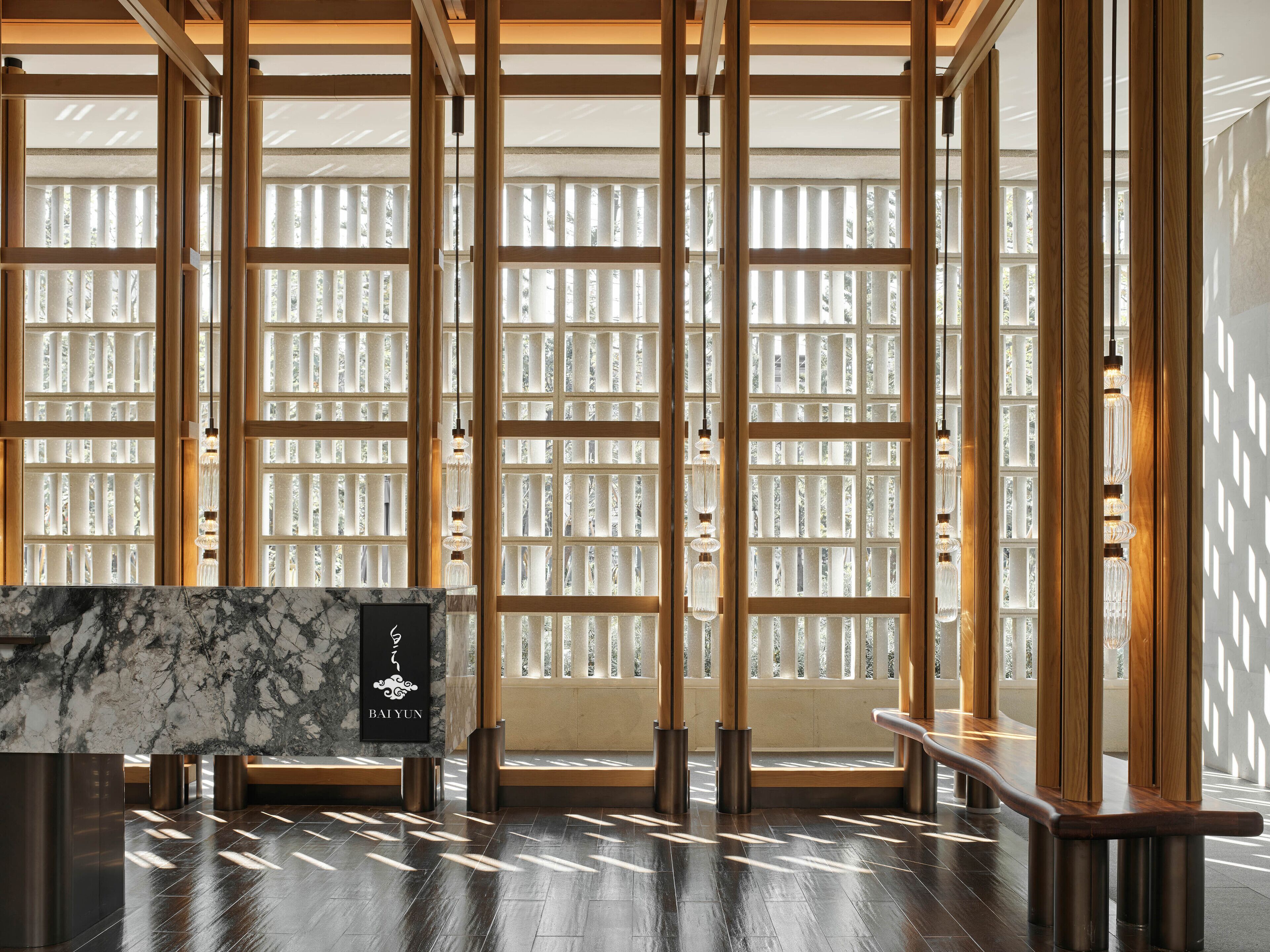 Decoração moderna com divisórias de madeira, uma receção de mármore e vista através de uma janela estampada.