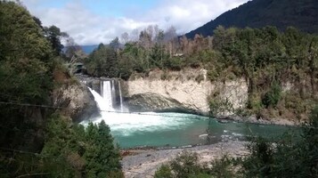 Uma cascata deságua em um rio, cercada por floresta densa e montanhas.