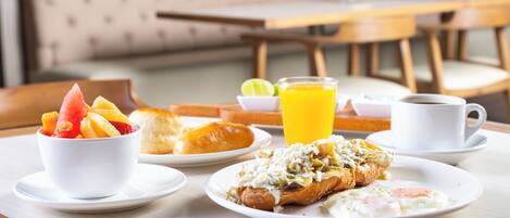 Disposição para o pequeno-almoço com uma tigela de fruta, croissant, omelete e café sobre uma mesa.