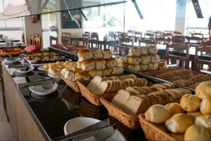 Buffet com diversos pães e pastelaria expostos em cestos.