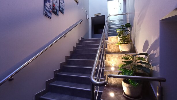 Uma escadaria com guarda-corpos de metal, plantas em vasos e uma placa indicando 'DEPARTAMENTOS'.