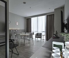 Quarto de hotel moderno com área de refeições, sofá e uma grande janela com cortinas.