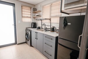 Cozinha compacta com máquina de lavar, pia, cafeteira e geladeira.