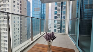 Varanda com mesa de madeira e um vaso de flores, vista para um horizonte urbano com edifícios modernos.