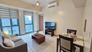Uma sala de estar moderna com sofá, mesa de centro, televisão e área de jantar.