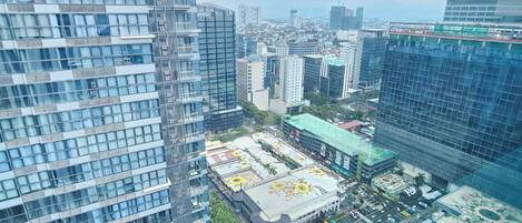 Um edifício alto com fachada de vidro moderna, cercado por outros edifícios altos e uma praça central com telhado verde e murais de girassóis.