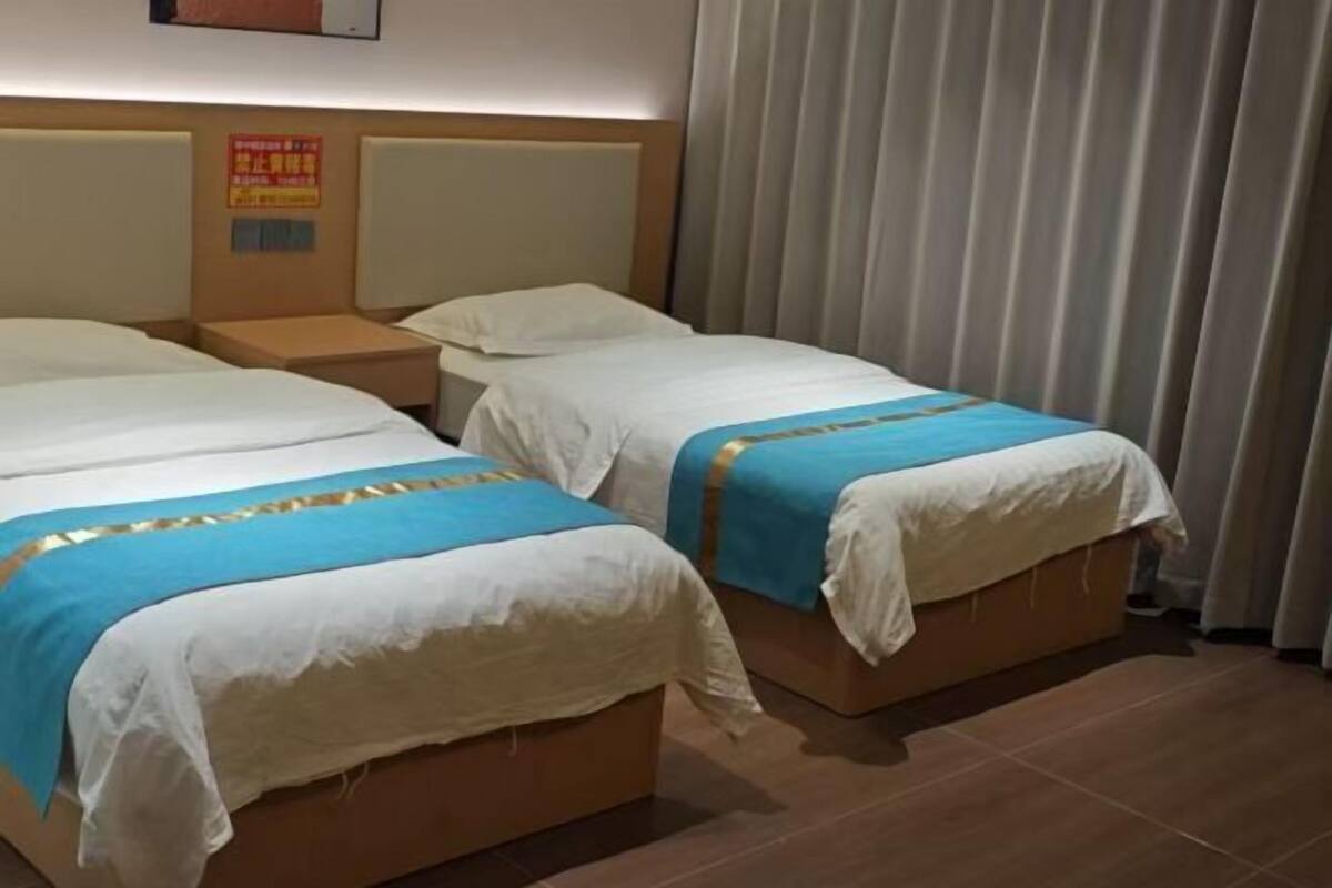 Quarto de hotel com duas camas, cabeceira, mesa de cabeceira e cortina.