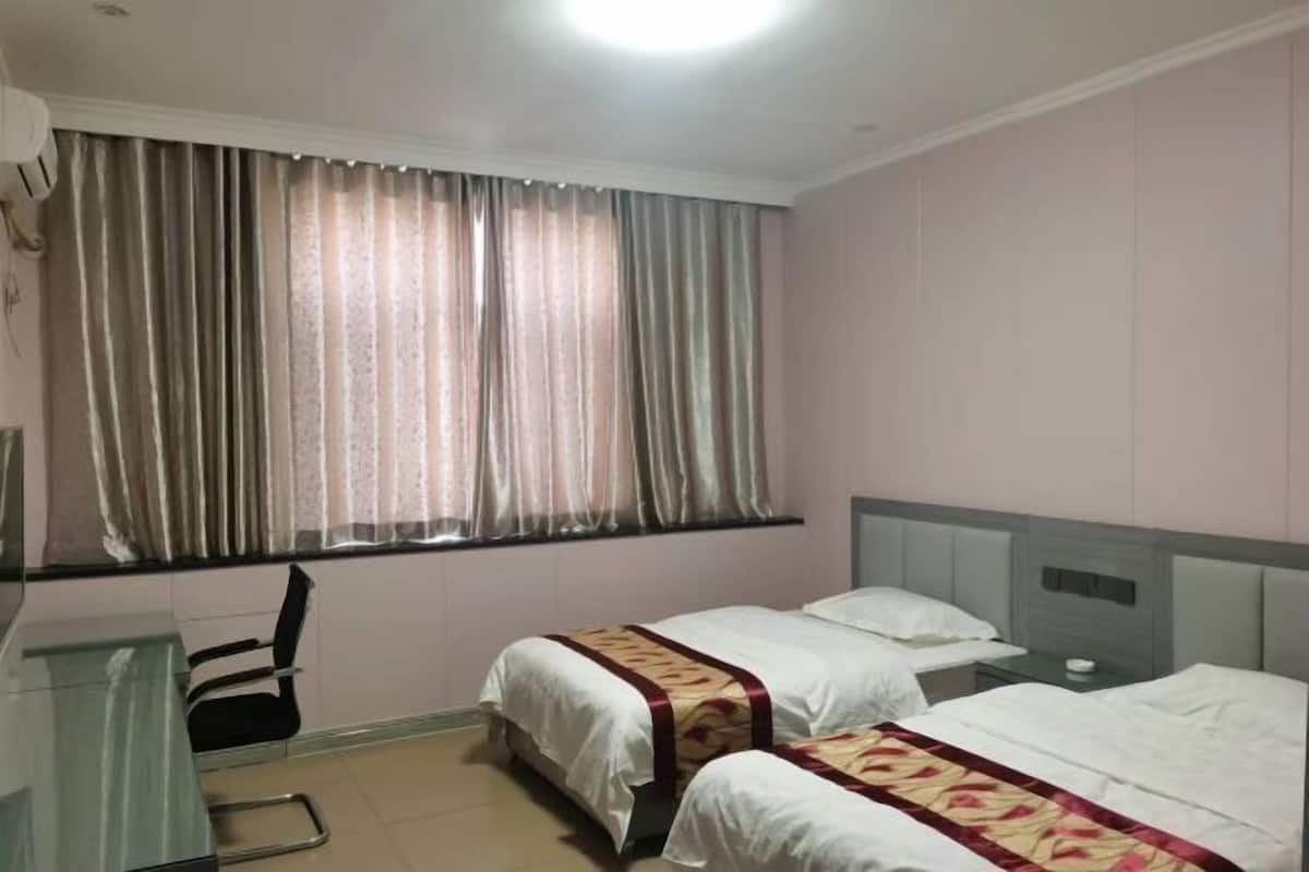 Quarto de hotel com duas camas, uma escrivaninha e uma cadeira.
