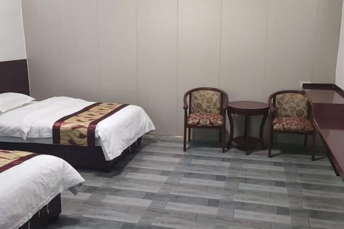 Quarto de hotel com duas camas, uma mesa pequena, duas cadeiras e uma escrivaninha de madeira.