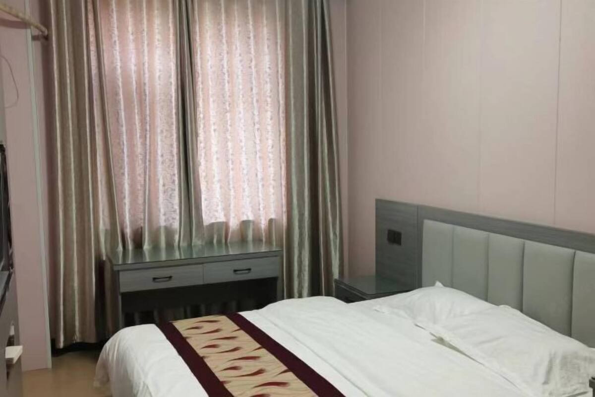 Quarto de hotel com cama, escrivaninha, cadeira e janela com cortinas.