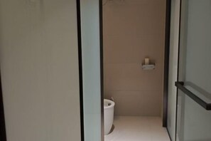 Corredor estreito que dá para um sanitário, com parede branca e um pequeno prateleira com um rolo de papel higiênico.