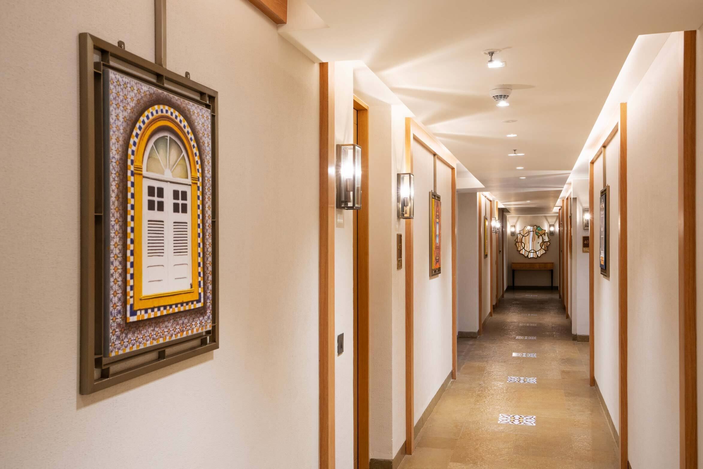 Um corredor de hotel com obras de arte emolduradas nas paredes, piso de madeira e teto com iluminação embutida.