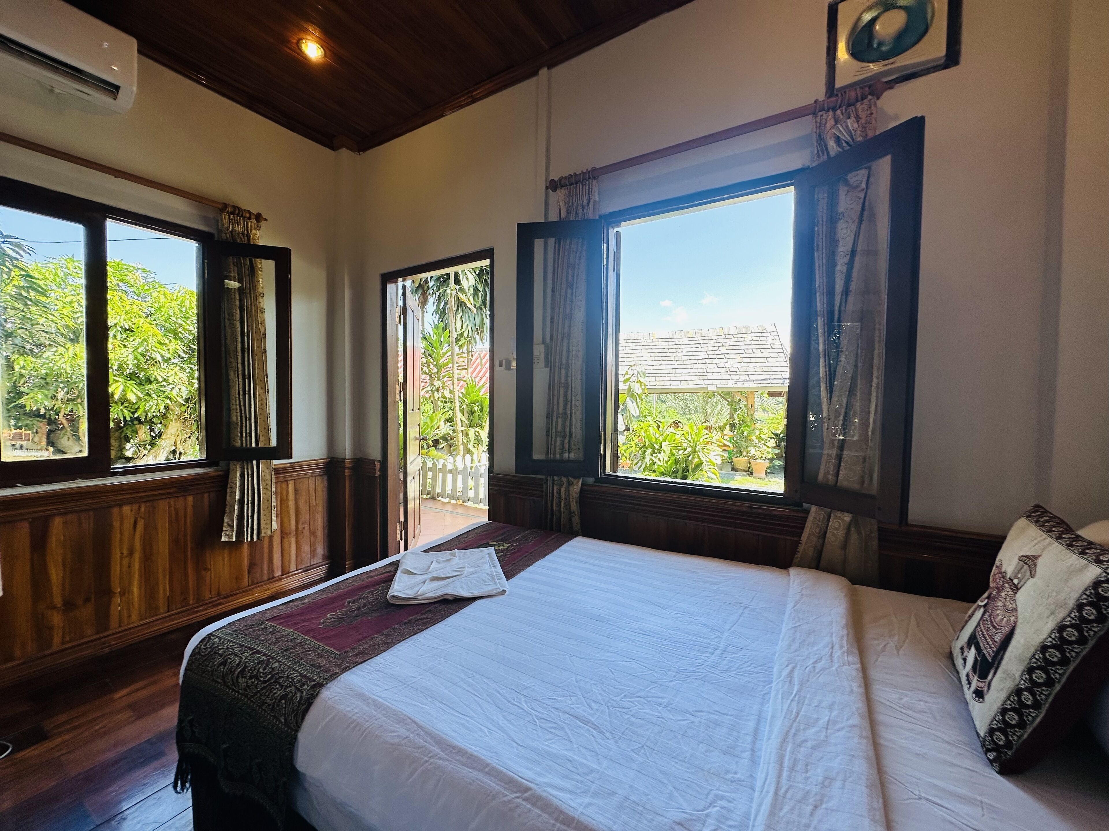 Quarto com uma cama grande, piso de madeira e duas janelas com cortinas.
