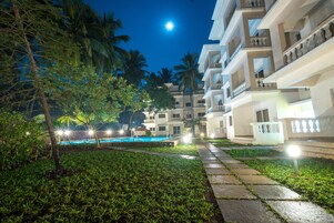 Um hotel com piscina, palmeiras e céu noturno com lua visível.