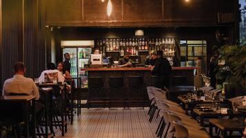 Interior de restaurante com luminárias pendentes, área de bar e disposição de mesas.