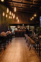 Interior de restaurante com luminárias pendentes, área de bar e disposição de mesas.