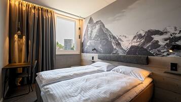 Quarto de hotel com uma cama grande, uma cadeira, uma mesa e uma janela com cortinas.