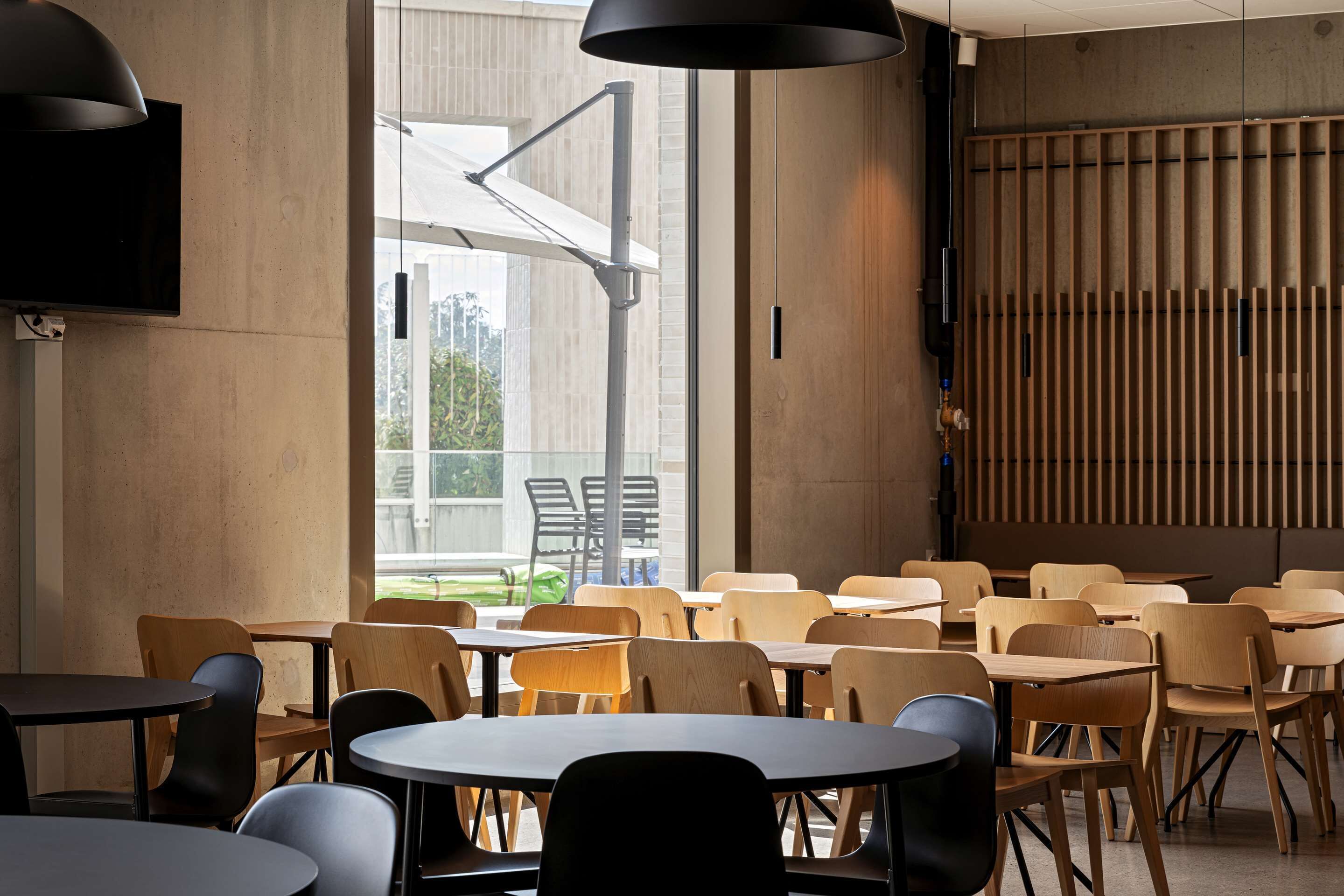 Uma sala de jantar moderna com mesas e cadeiras, janelas amplas e vista para o exterior.