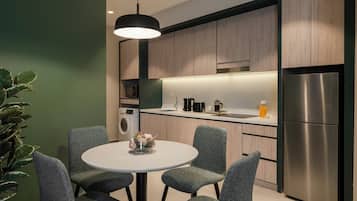 Uma cozinha moderna com uma mesa de jantar redonda, quatro cadeiras, uma cafeteira, uma geladeira e um pendente.