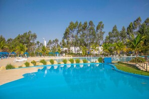 Piscina com espreguiçadeiras e guarda-sóis, cercada por palmeiras e céu claro.