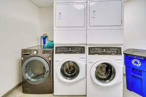 Uma lavanderia com máquinas de lavar empilhadas e uma lixeira azul para reciclagem.