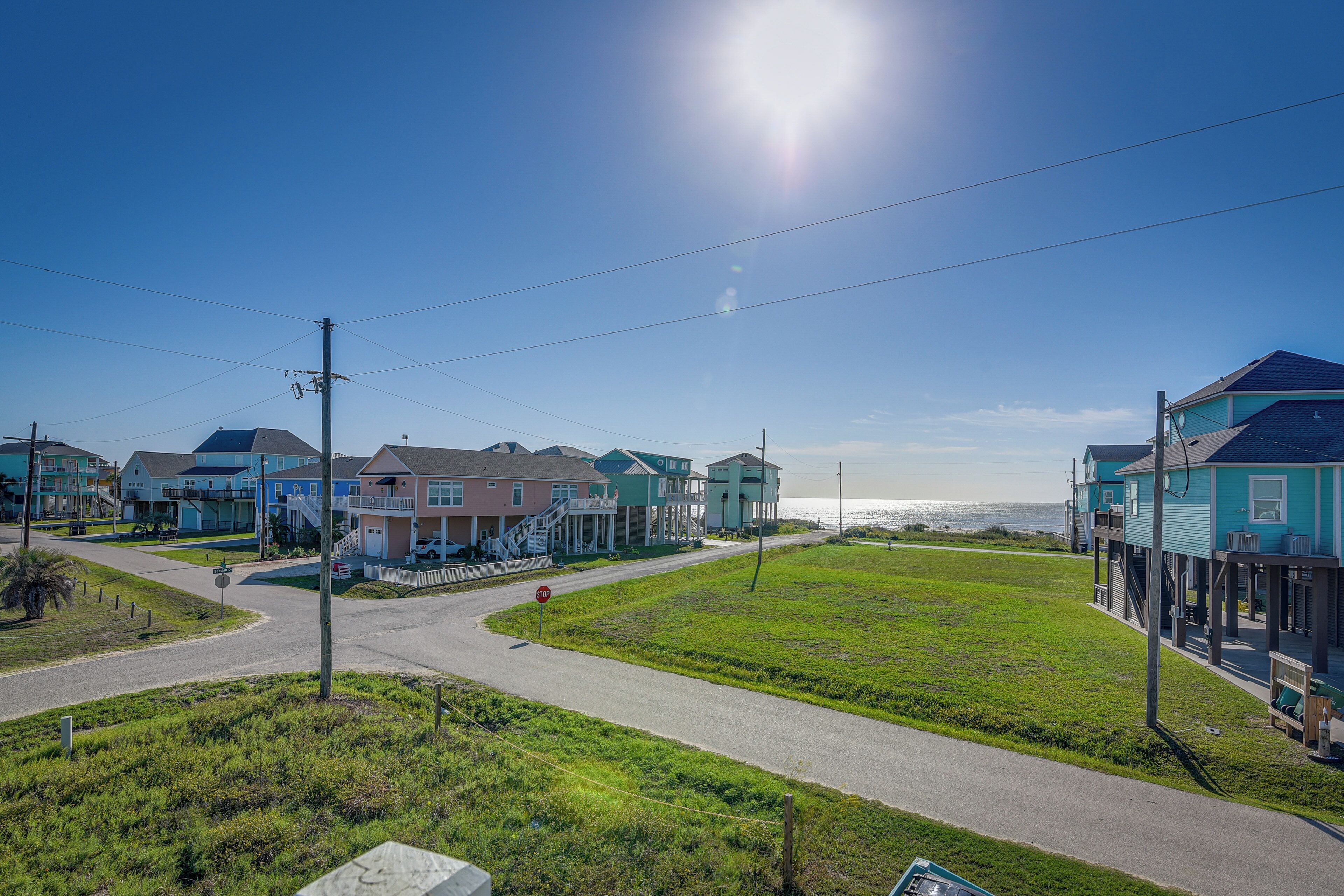 Área residencial costeira com casas ao longo da orla, céu claro e uma estrada que leva à praia.