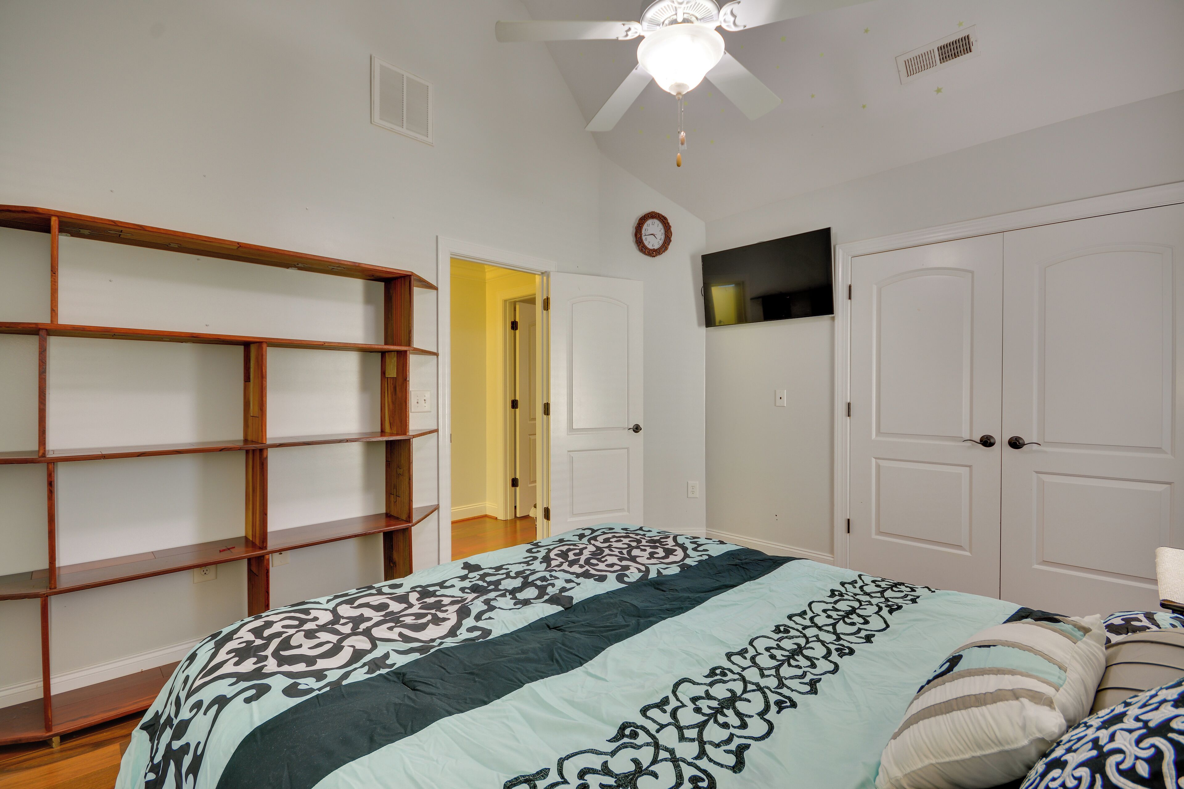 Quarto com uma cama, guarda-roupa, ventoinha no teto e porta que dá para outro cômodo.