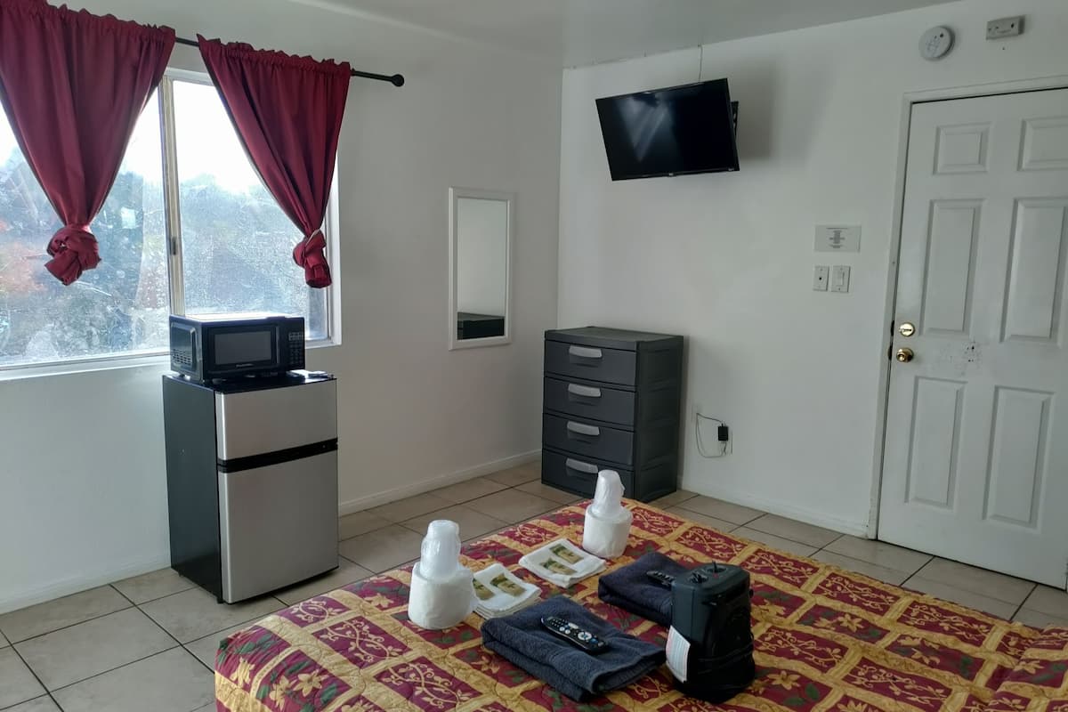 Quarto com cama, televisão, penteadeira, micro-ondas e janela com cortinas.