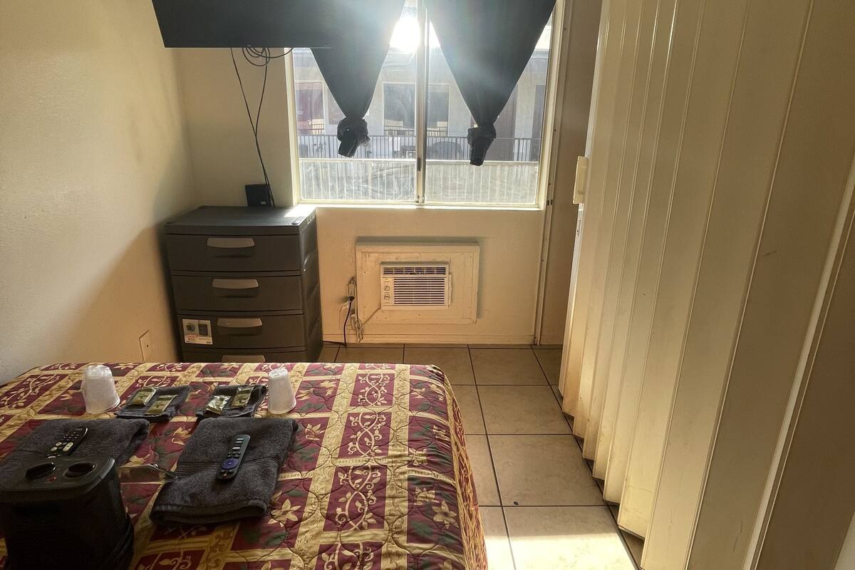 Quarto com cama, cômoda, janela com cortinas e radiador.