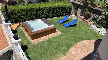 Um quintal com banheira de hidromassagem, duas poltronas de descanso, gramado bem cuidado e muro de pedra.