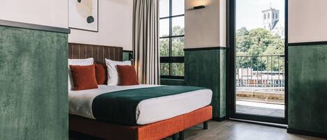 Quarto de hotel moderno com uma cama grande, vista para a paisagem urbana pela janela e uma parede de destaque verde.