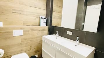 Casa de banho moderna com soalho de madeira, lavatório branco duplo, espelho grande e sanita.