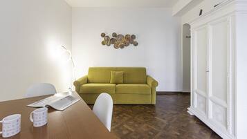Um quarto com uma mesa de jantar de madeira, duas cadeiras brancas, um sofá verde, um objeto decorativo na parede e um armário branco.